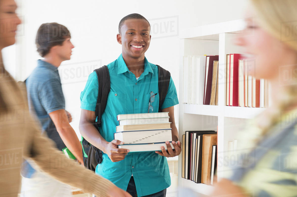Teenage boy carrying books in library - Royalty-free Stock Photo | Dissolve