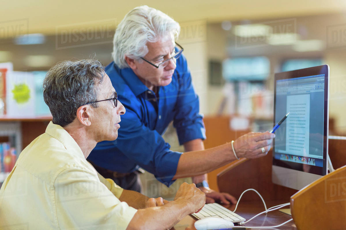 Teacher helping adult student use computer in library - Stock Photo ...