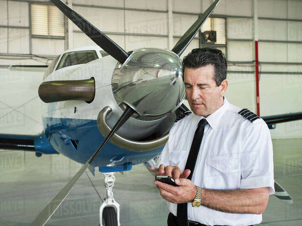 Caucasian pilot using cell phone in hangar - Stock Photo - Dissolve