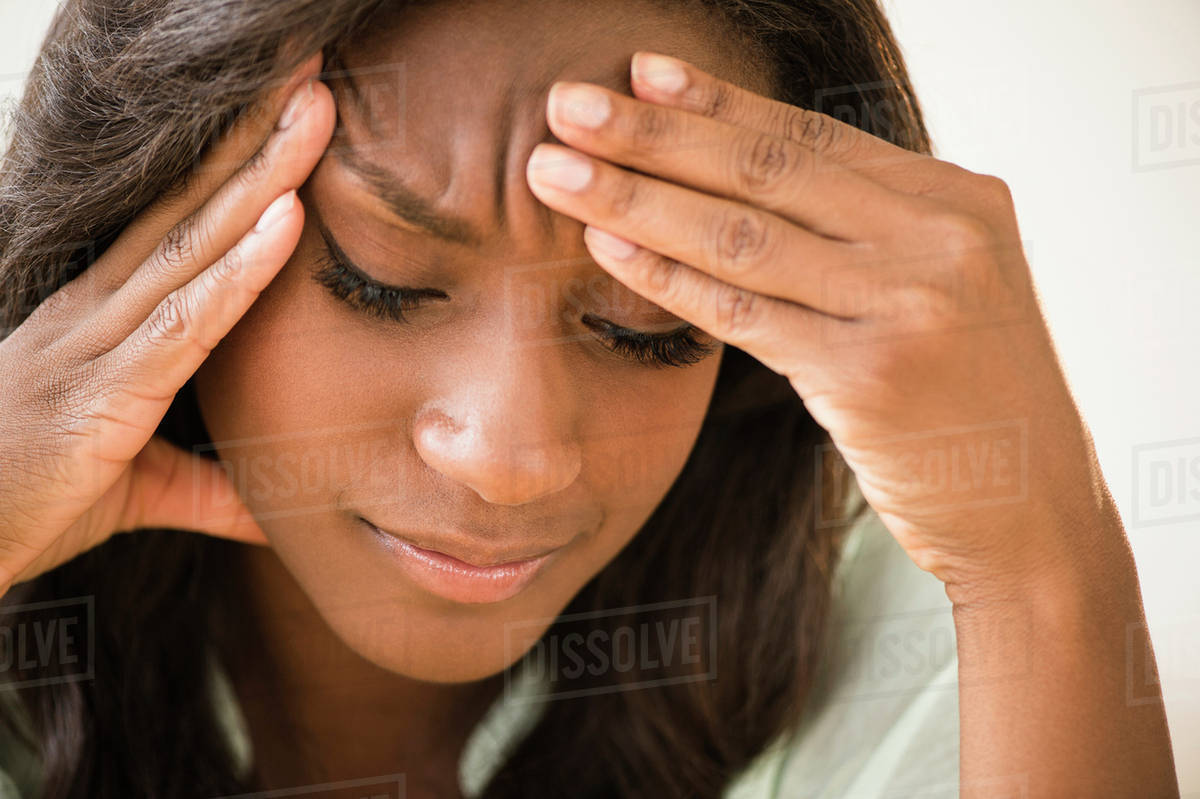 Black woman frowning with head in hands - Stock Photo - Dissolve