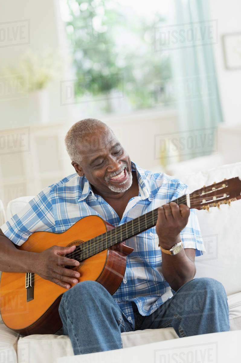 Black man playing guitar on sofa - Stock Photo - Dissolve