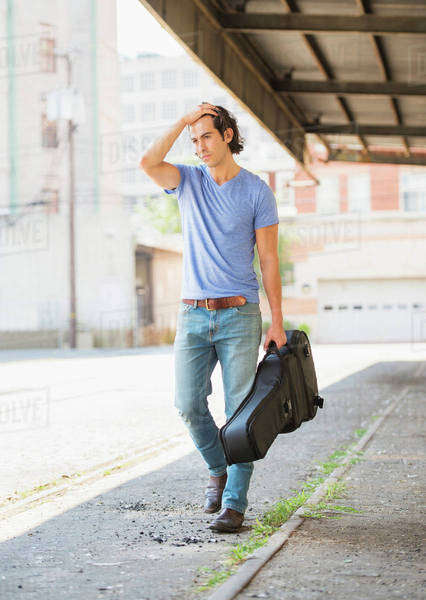 Caucasian man carrying guitar case on city street - Royalty-free Stock ...