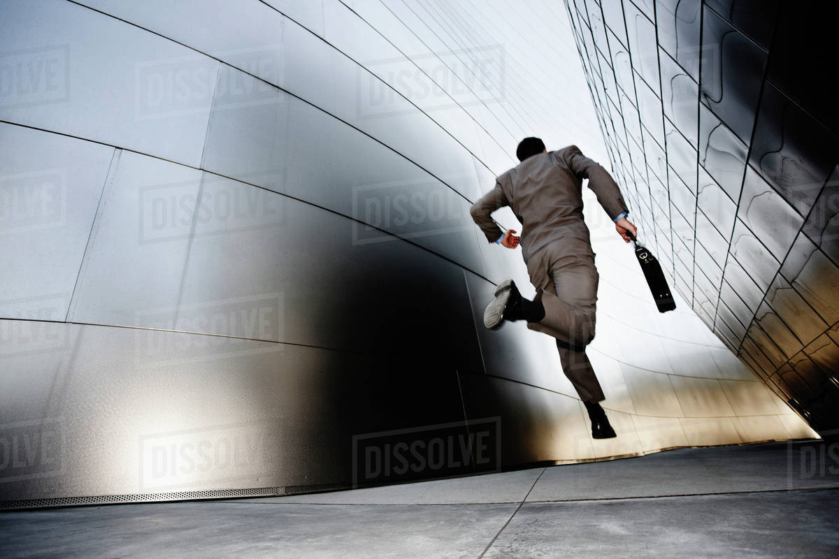 Businessman running down urban alley - Stock Photo - Dissolve