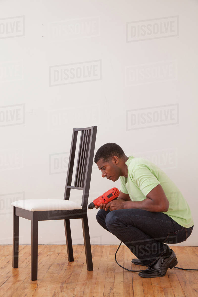 Black man using drill on chair - Stock Photo - Dissolve