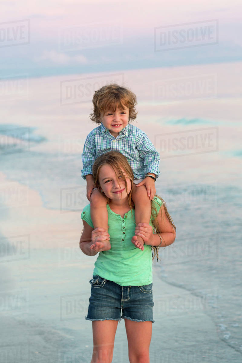 Caucasian girl carrying brother on shoulders on beach - Stock Photo ...