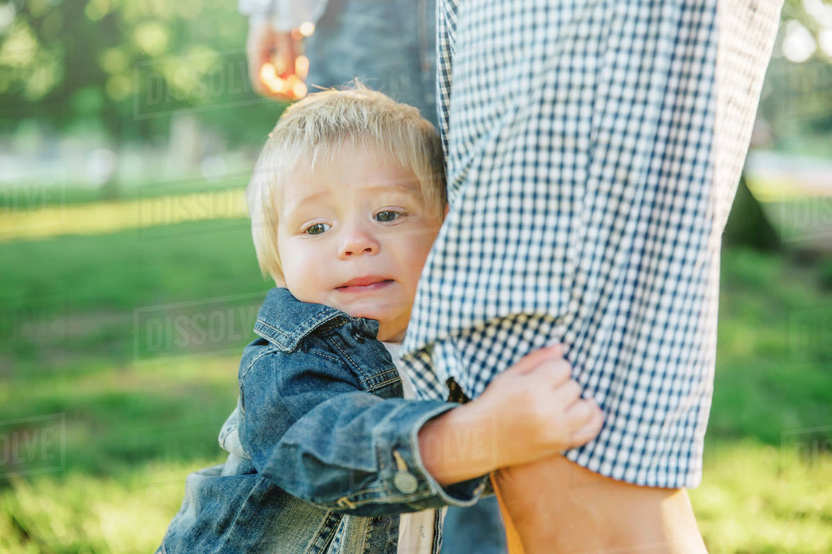Boy clutching leg of father in grass in park - Stock Photo - Dissolve