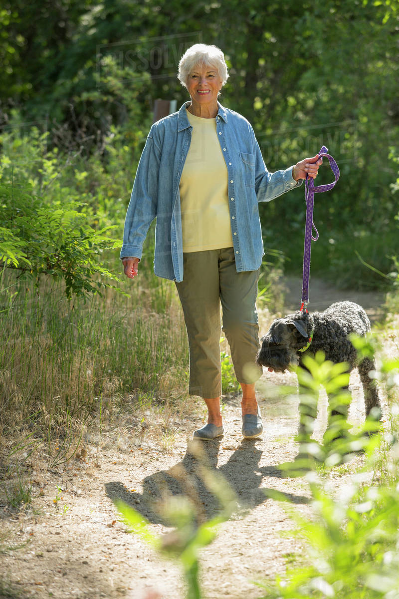 Older Caucasian woman walking dog on dirt path - Stock Photo - Dissolve