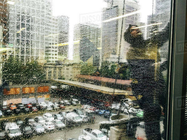 Window washer cleaning rainy window of office building - Stock Photo ...