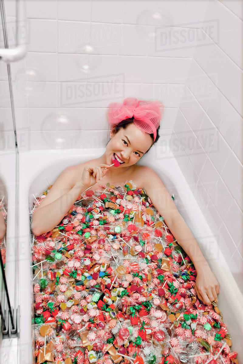 Mixed race woman taking a bath in candy - Stock Photo - Dissolve