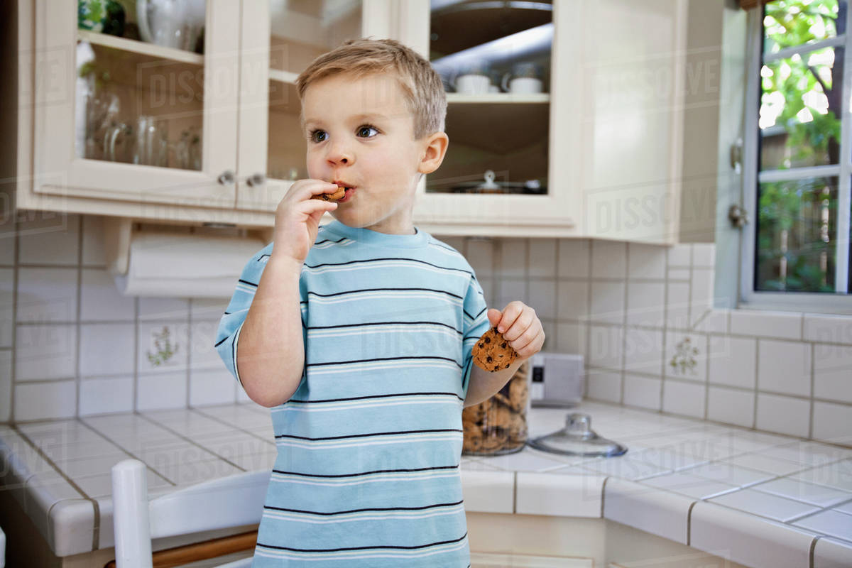 Caucasian boy eating cookie in kitchen - Royalty-free Stock Photo ...