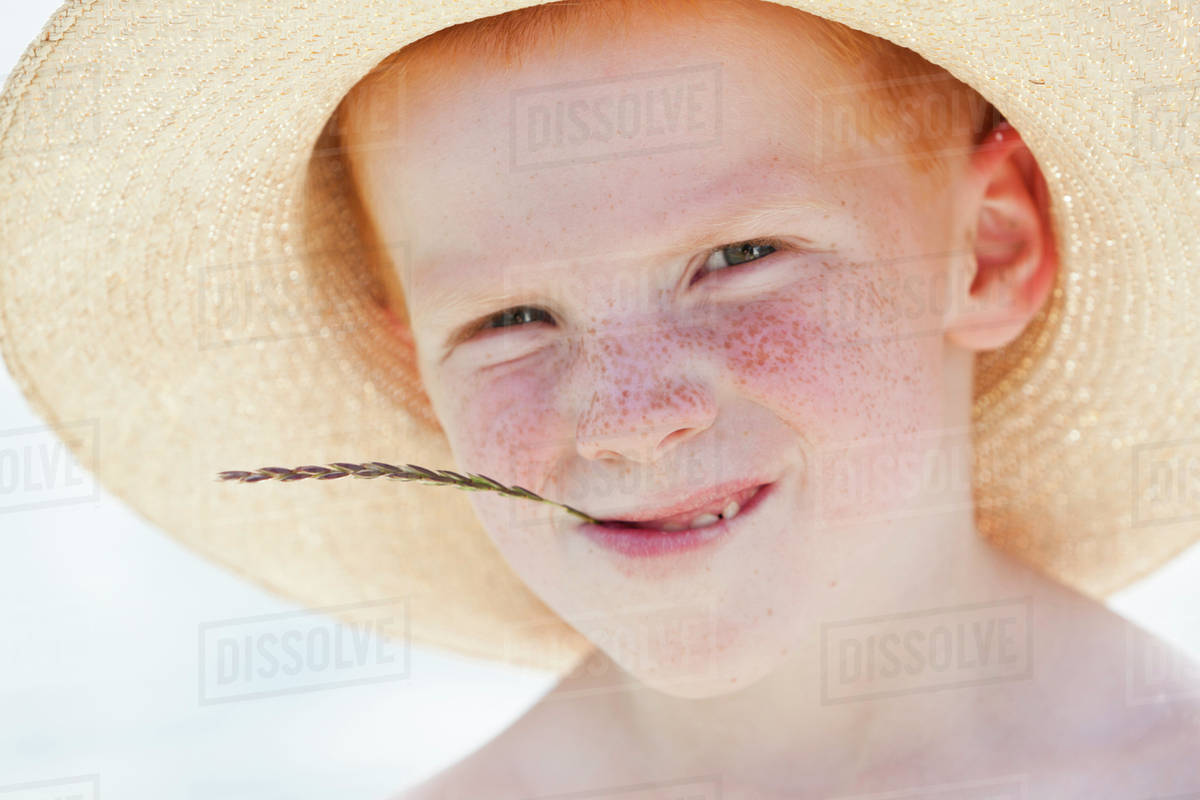 Freckled boy in hat chewing on straw - Royalty-free Stock Photo | Dissolve