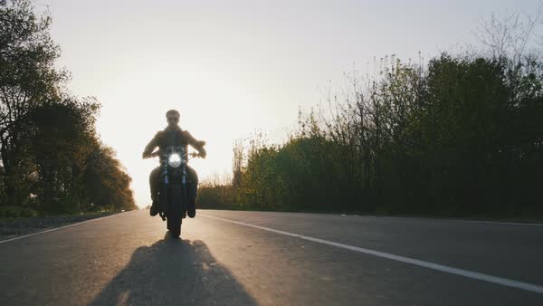 Motorcyclist driving and surfing on his motorbike on the road in sun ...