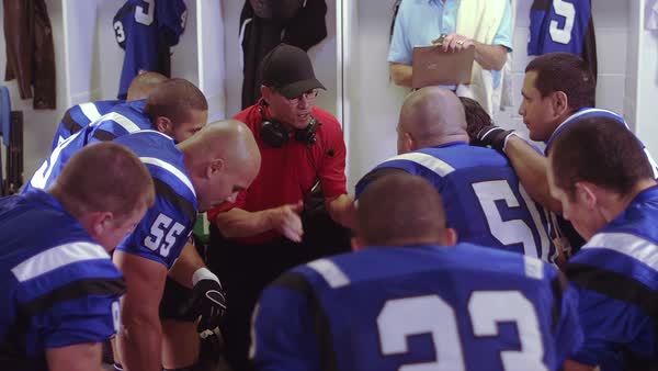 Football players sit in a circle in the locker room and coach gives a ...