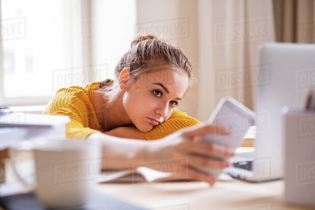 A young happy college female student sitting at the table at home ...