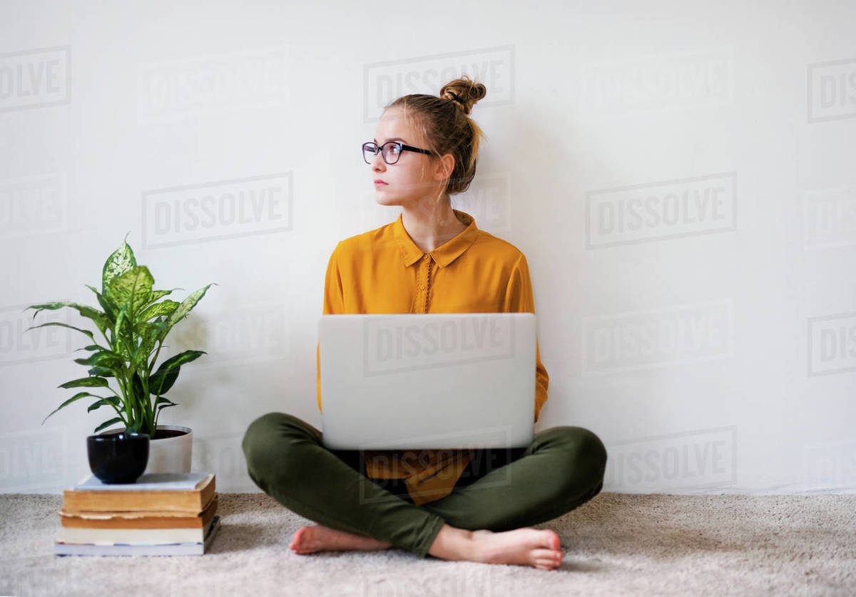 A young college female student sitting on floor at home, using laptop ...