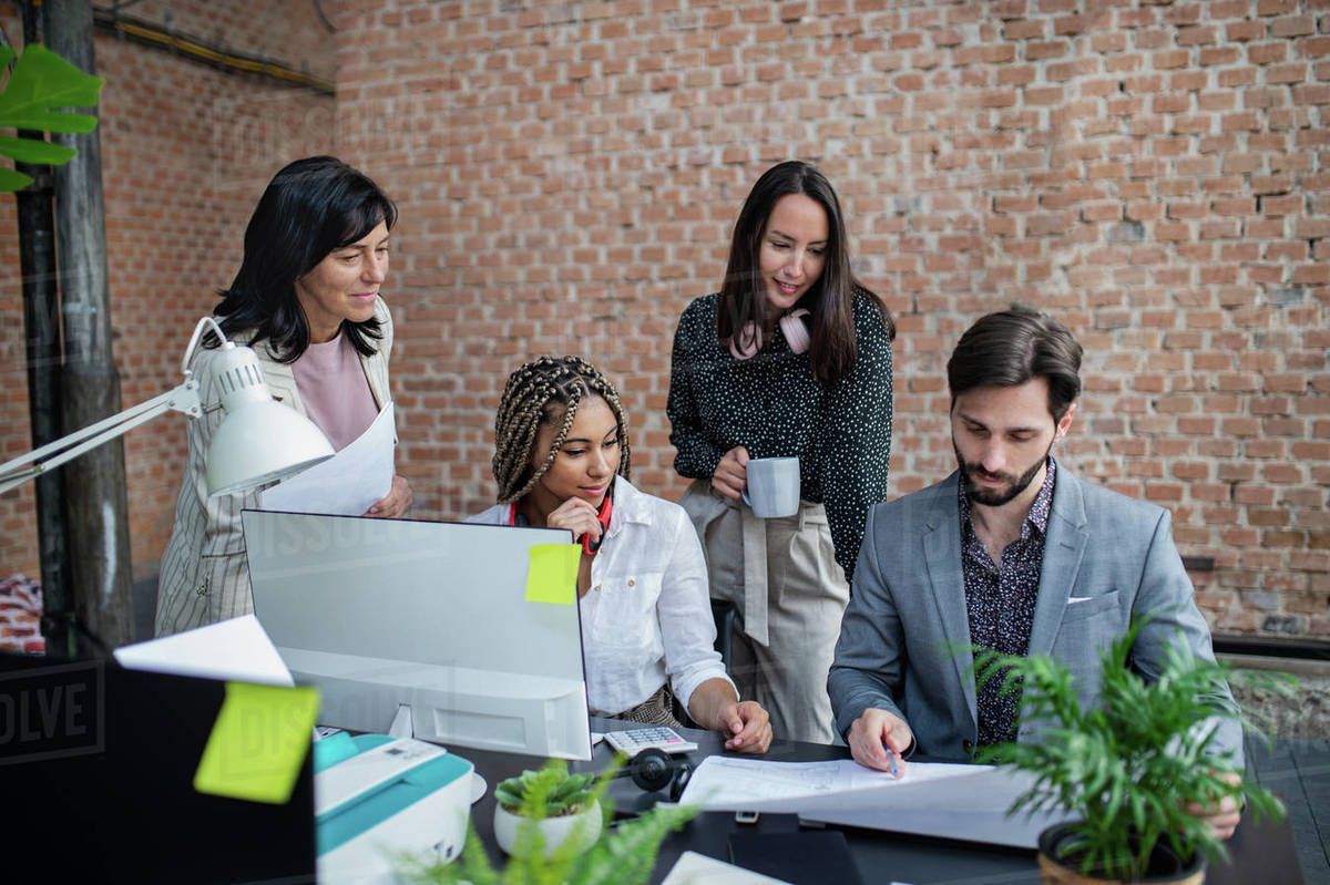 Happy young and old businesspeople sitting and working at desk in ...