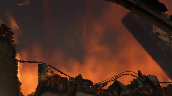 Behind smoldering siding, flames rage in the interior of a house gutted ...