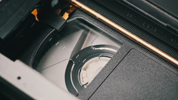 VHS cassette is played inside a VCR tape recorder, top view. Videotape ...