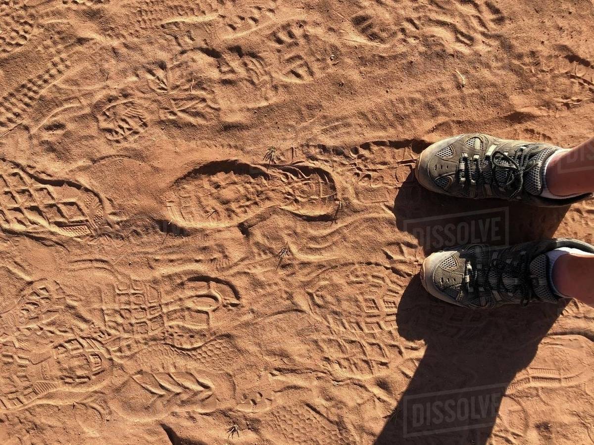 Shot looking down on feet standing in red dirt with footprints ...