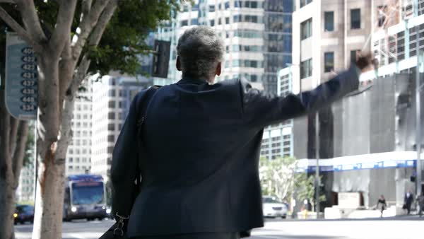 Older business woman tries to hail a bus downtown, but it drive right ...