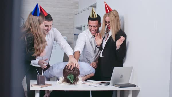 Office workers in party hats smashing face of their colleague into the ...