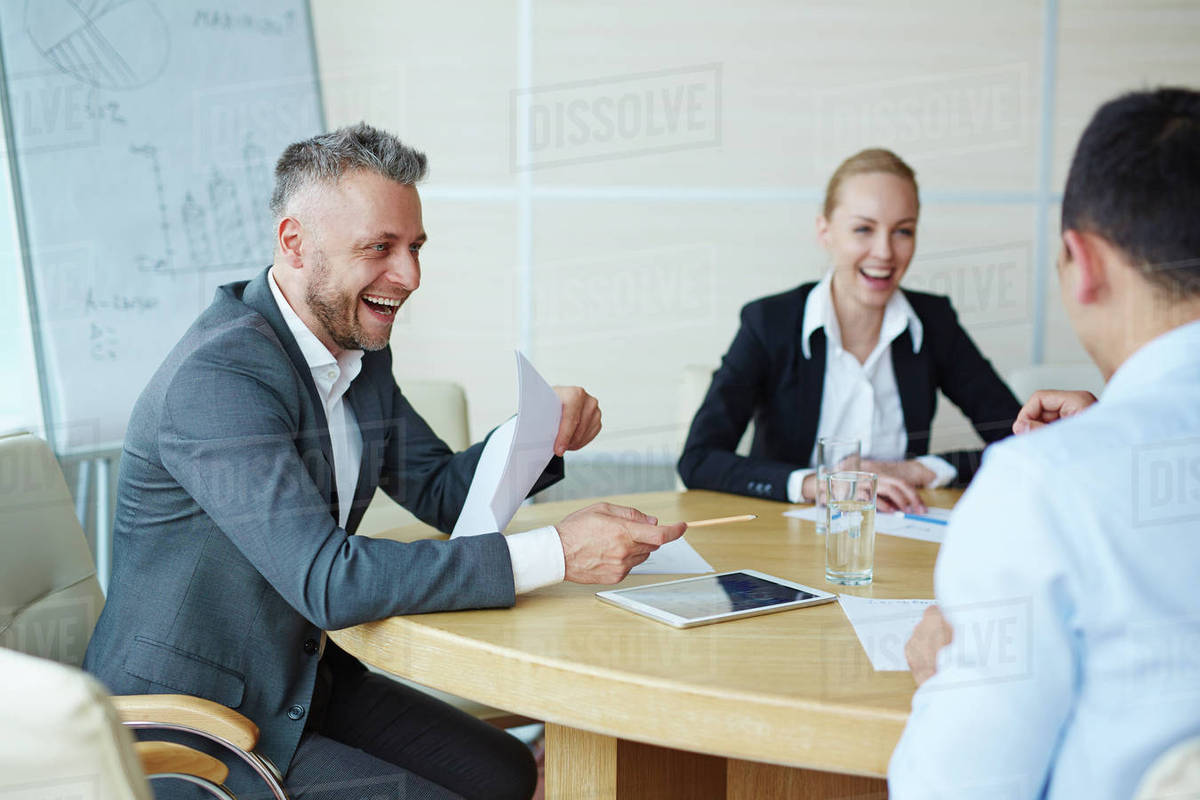 Laughing businessman with paper talking to colleagues in office - Stock ...