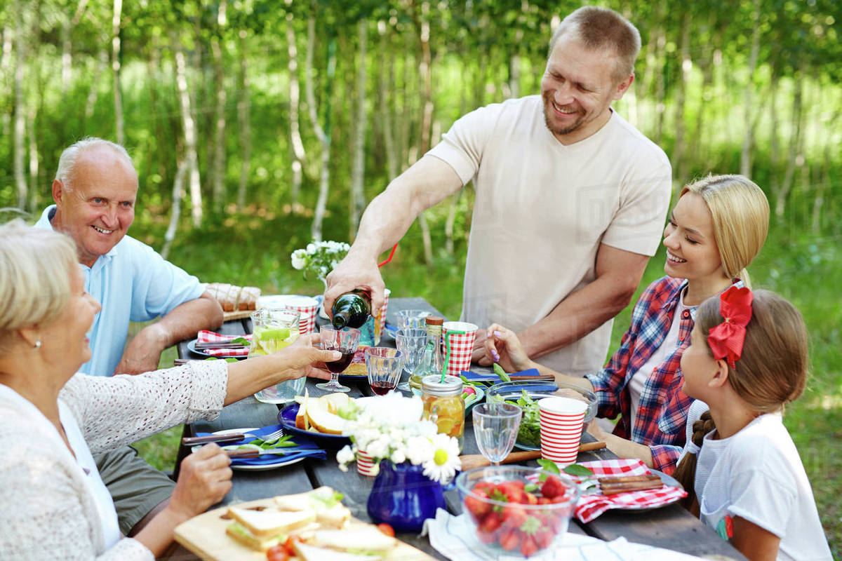 Big family sitting around table and having dinner in natural ...
