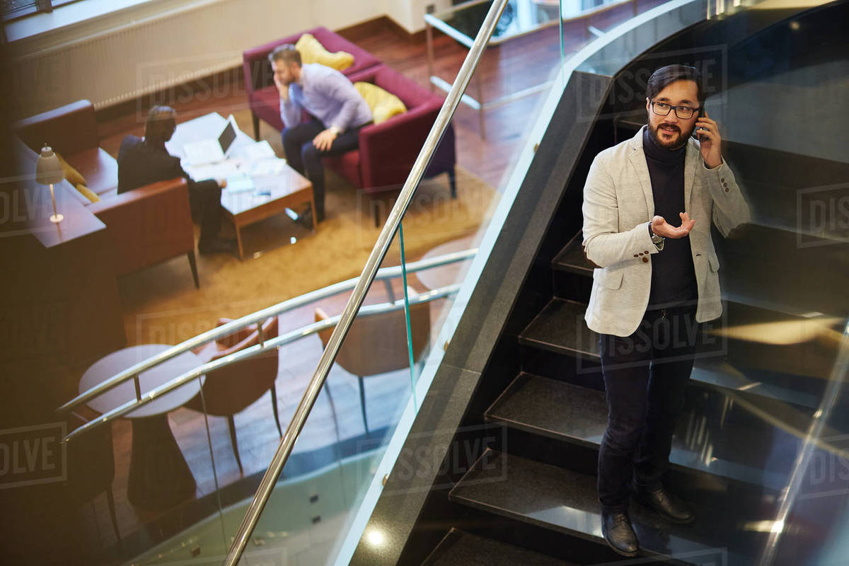 Modern employee speaking on the phone on stairs inside office center ...