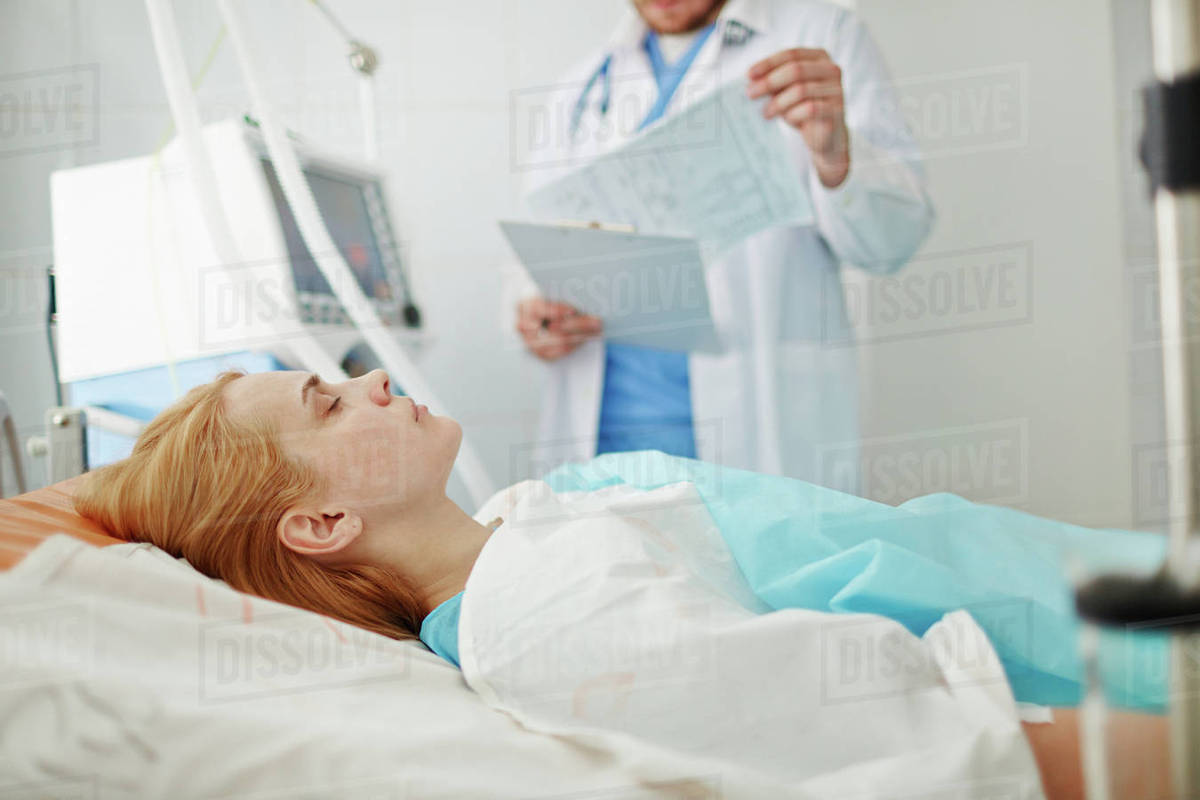 Unconscious woman lying on bed in hospital with doctor standing nearby ...