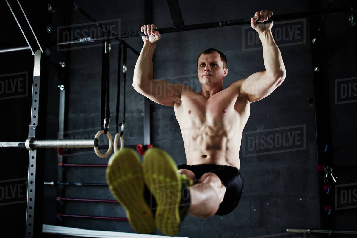 Muscular man doing pull-ups in gym - Stock Photo - Dissolve