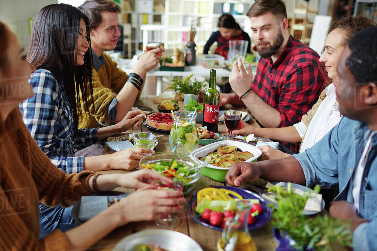 Group of happy friends sitting by table and having dinner - Royalty ...