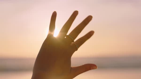 Close up woman hand reaching for sunlight on beach playing with golden ...