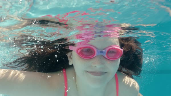 Happy girl swimming underwater in pool smiling waving hand enjoying ...