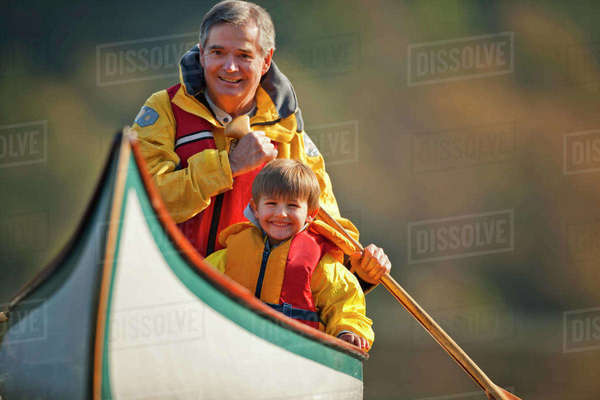 Happy grandfather and young grandson canoeing together on a lake ...