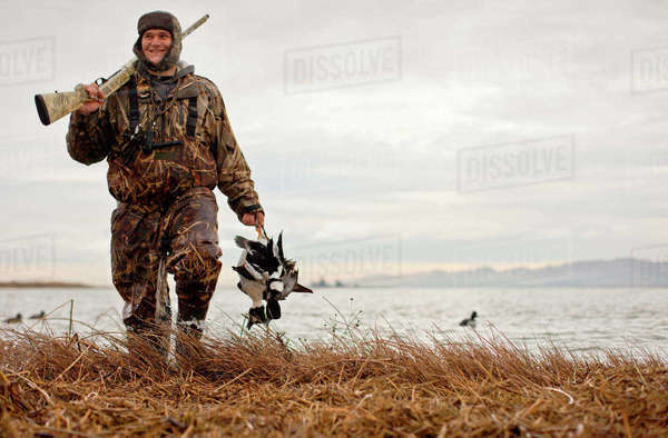 Satisfied duck hunter wearing camouflage clothing carrying two dead ...
