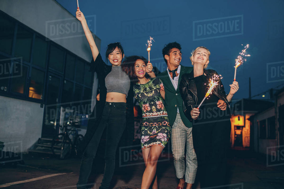 Shot of young friends walking on city street at night with fireworks ...