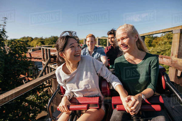 Shot of young friends riding roller coaster. Young people having fun at ...