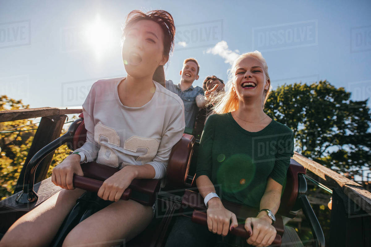 Enthusiastic young friends on roller coaster ride. Young people having ...