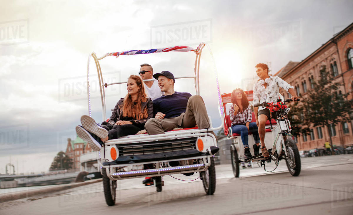 Group of young people enjoying tricycle ride in the city. Smiling ...