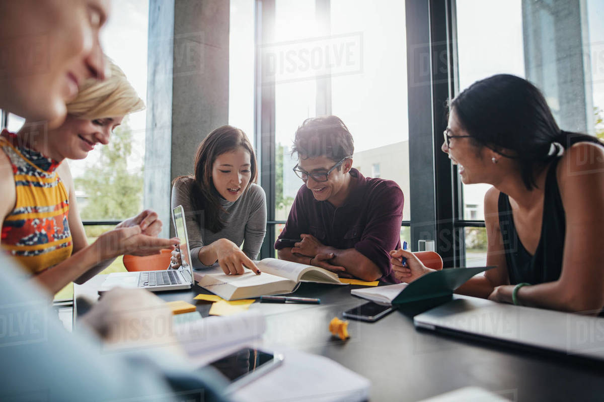 Young students sitting at a table in a library and reading books for ...