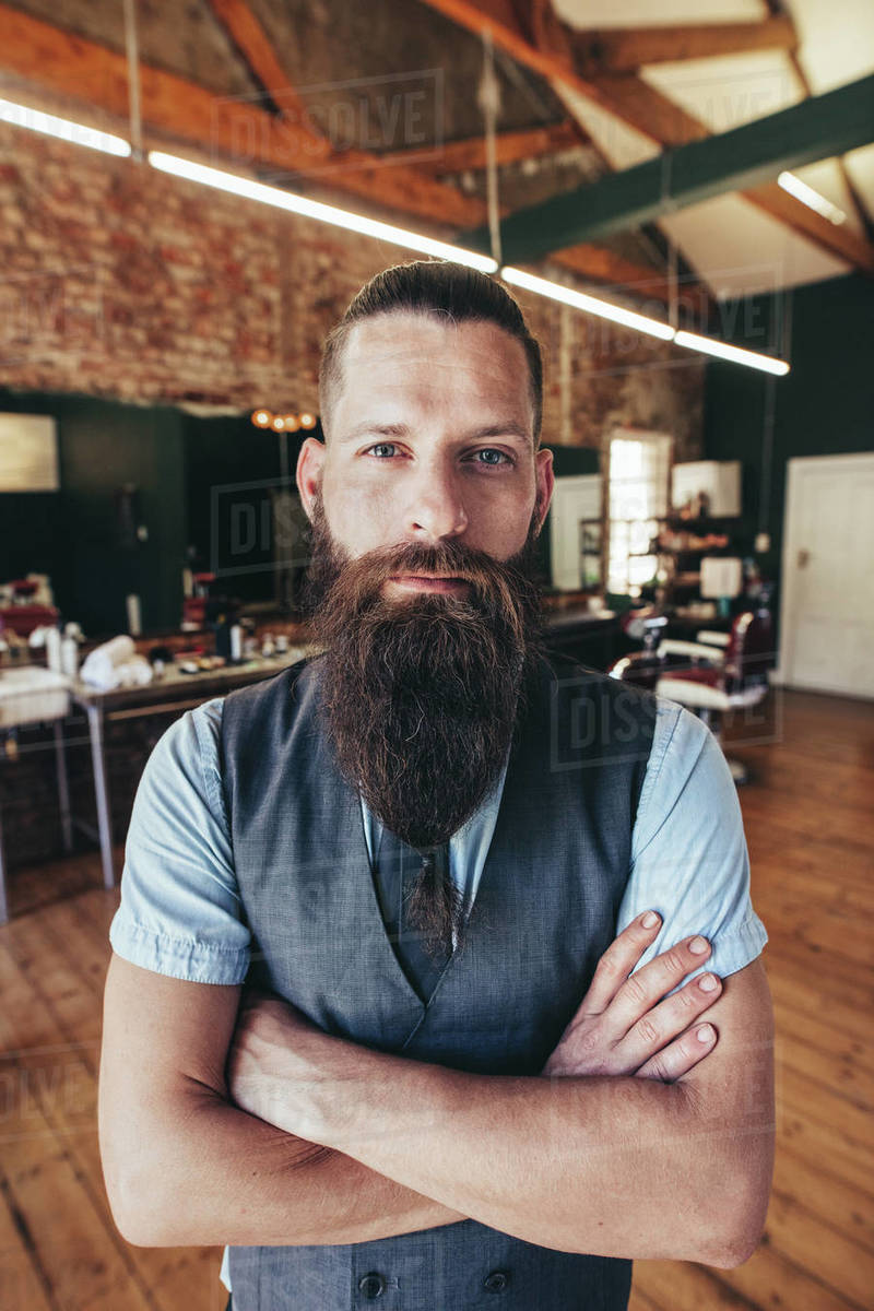 Portrait of stylish male barber with beard standing with his arms ...