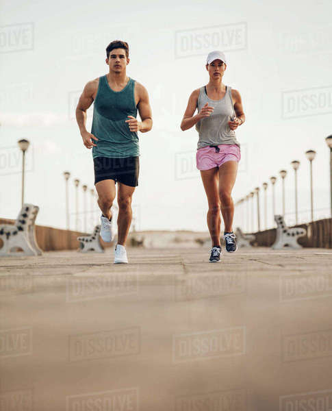 Two young people running on road. Couple of runners on morning run ...