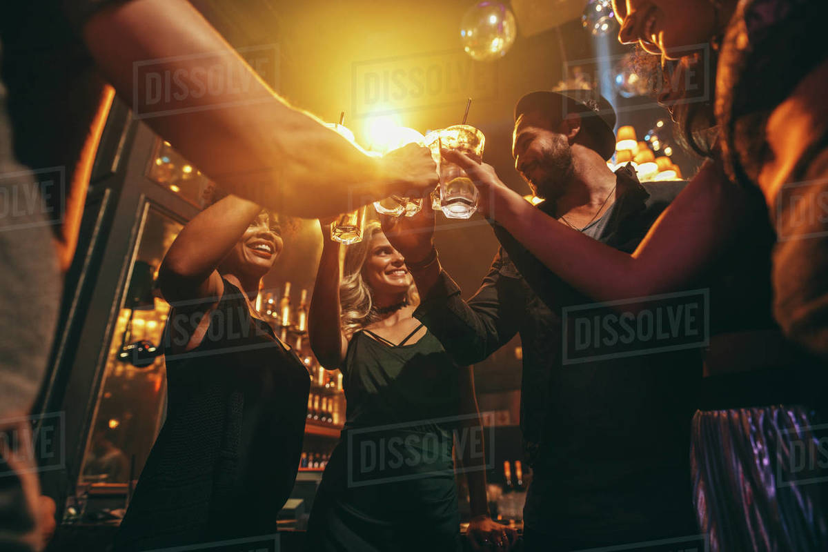 Low angle shot of group of friends enjoying drinks at bar together ...