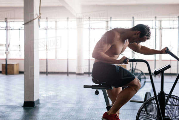 Muscular athlete doing intense workout on gym bike. Fitness man ...