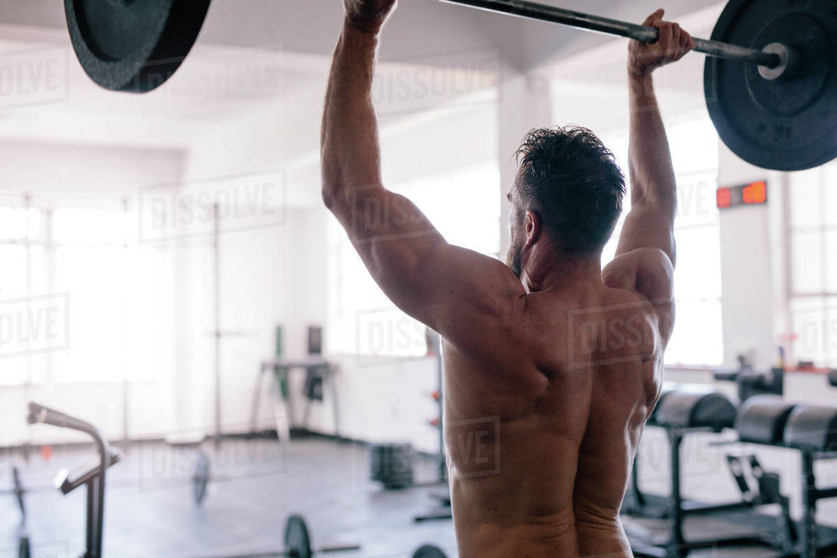 Rear view shot of healthy cross training man performing deadlift in gym ...