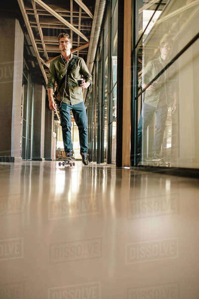 Full length shot of young man skateboarding in office. Casual ...