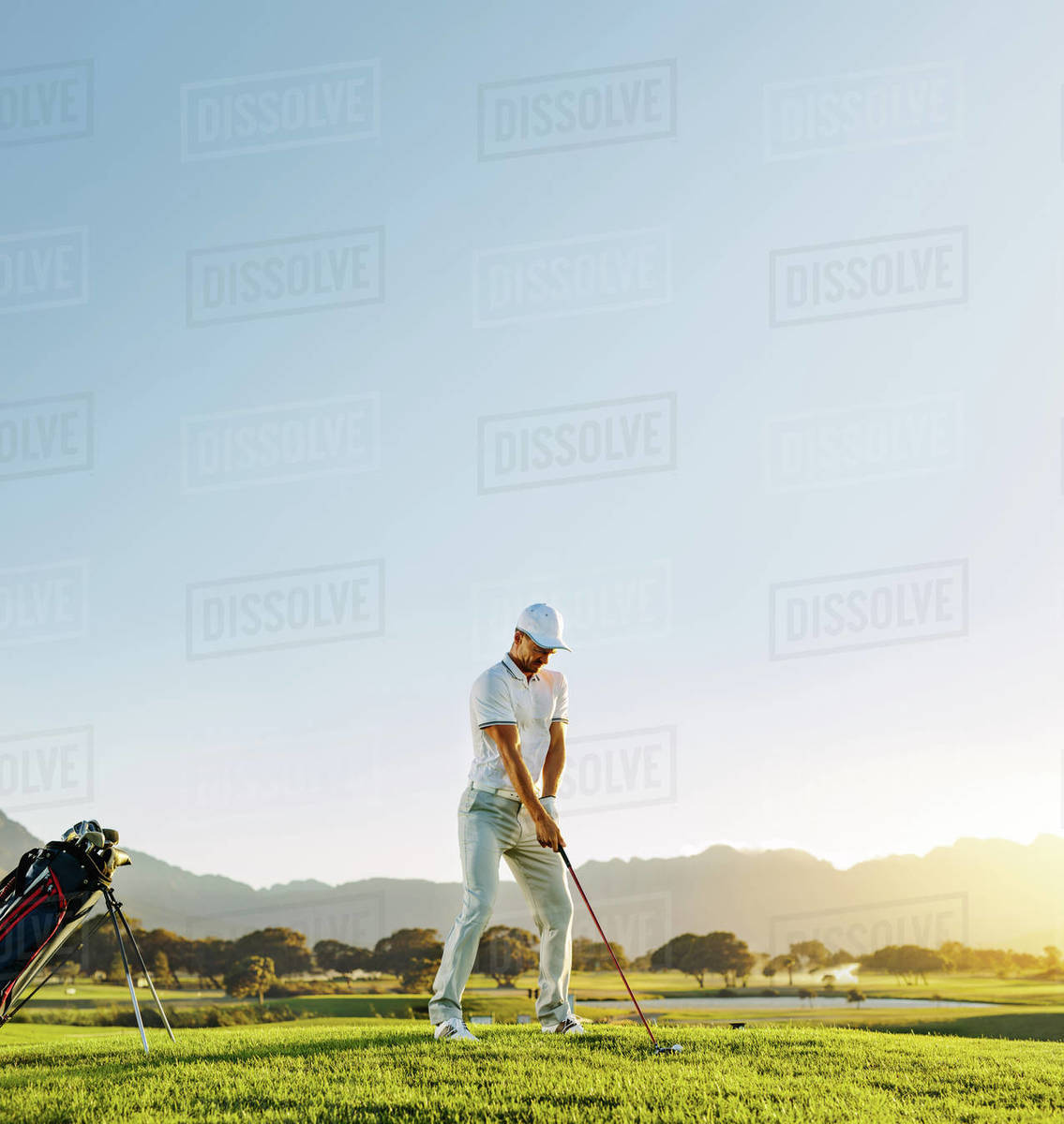 Full length of male golfer taking shot while standing on golf course ...