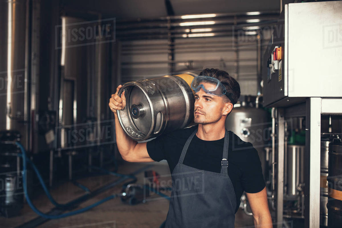 Brewer with large metal container at brewery factory. Young man working ...