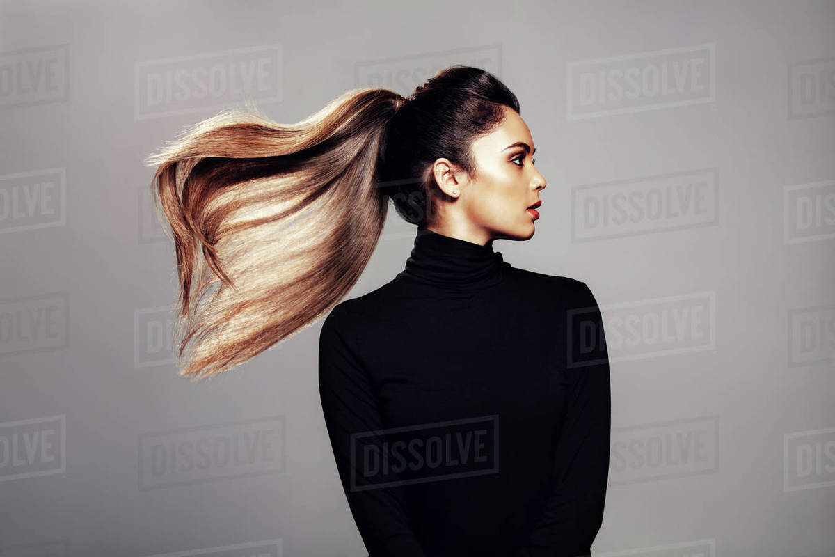 Studio shot of stylish young woman with flying hair against grey ...