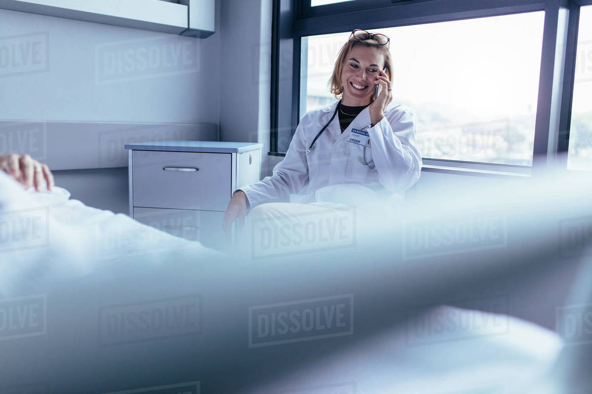Happy female doctor sitting in hospital room and making a phone call ...